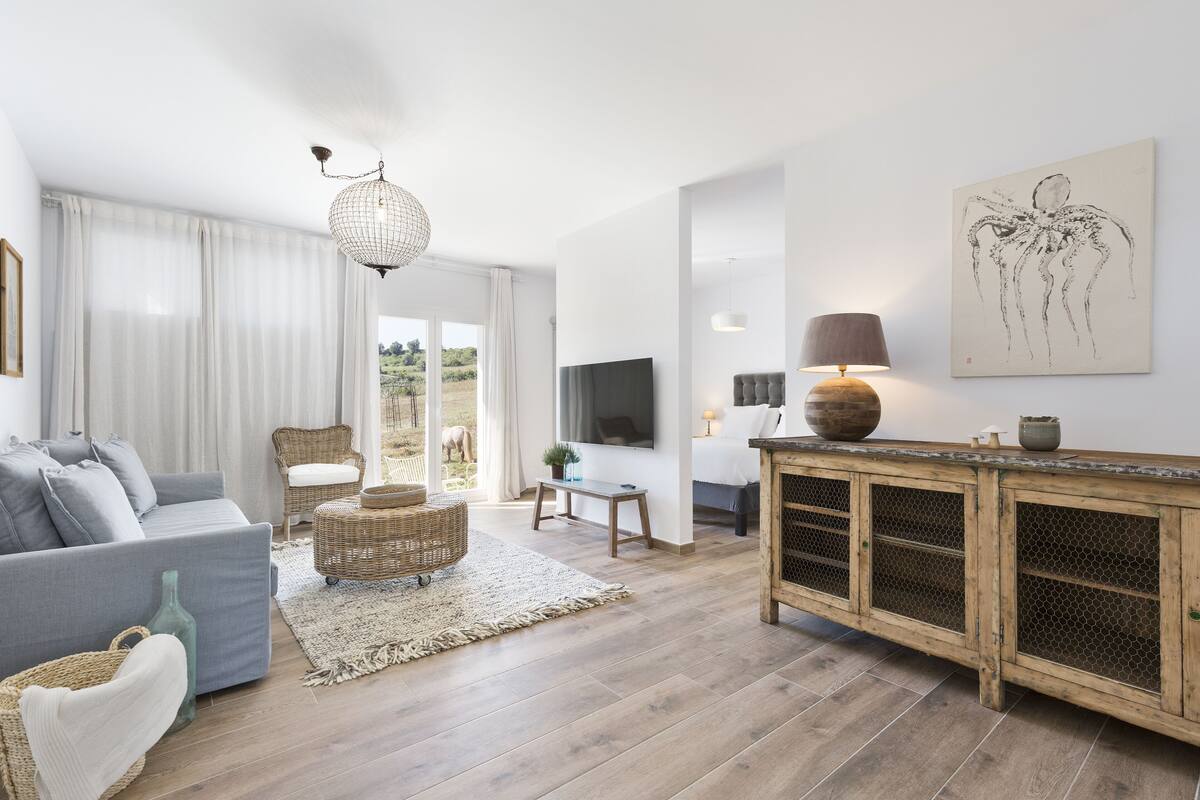 Uma sala de estar moderna com um sofá cinza, mobiliário de vime, um armário de madeira e uma grande janela com cortinas.