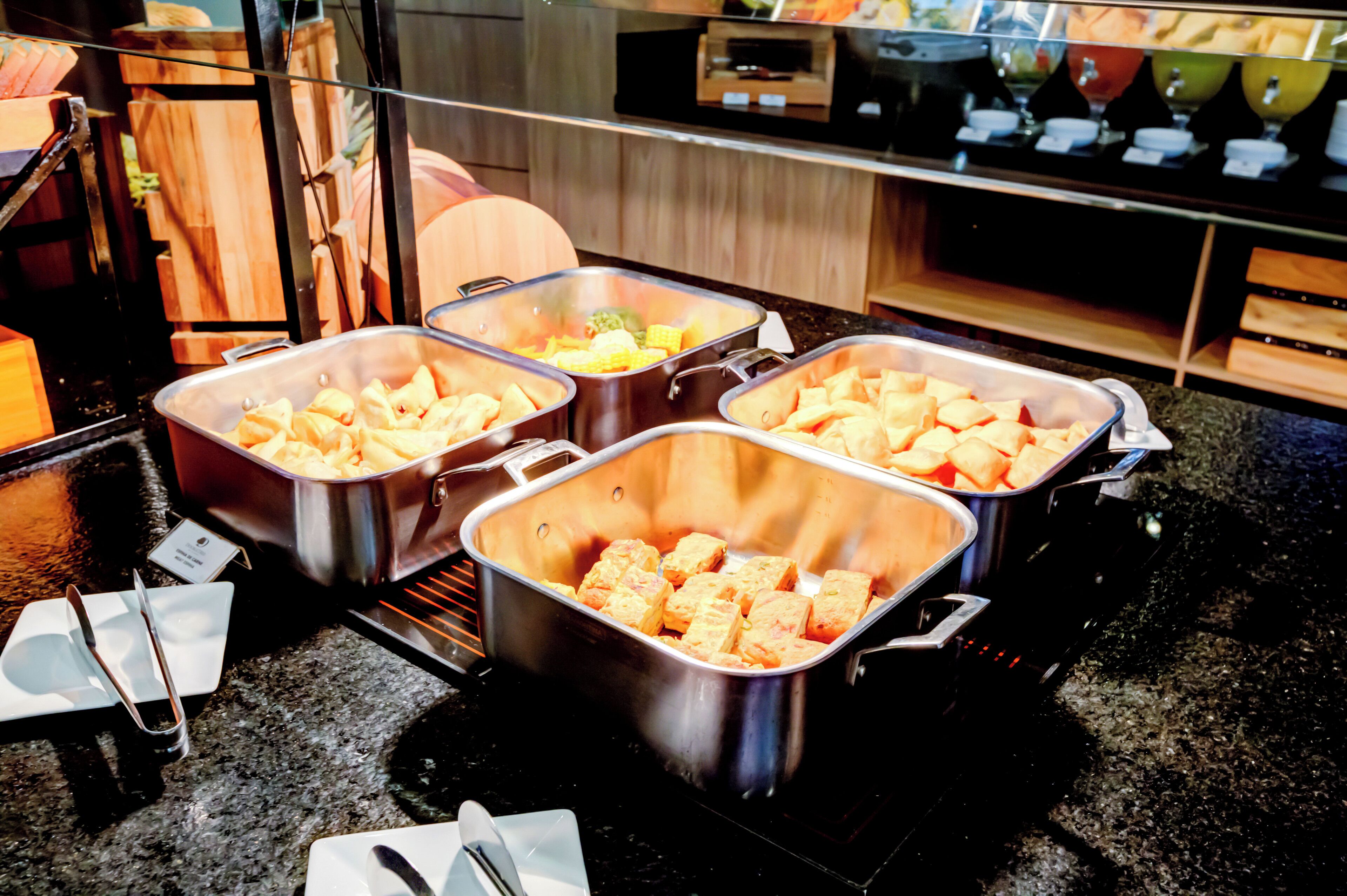 Buffet com diversos alimentos em recipientes de metal.