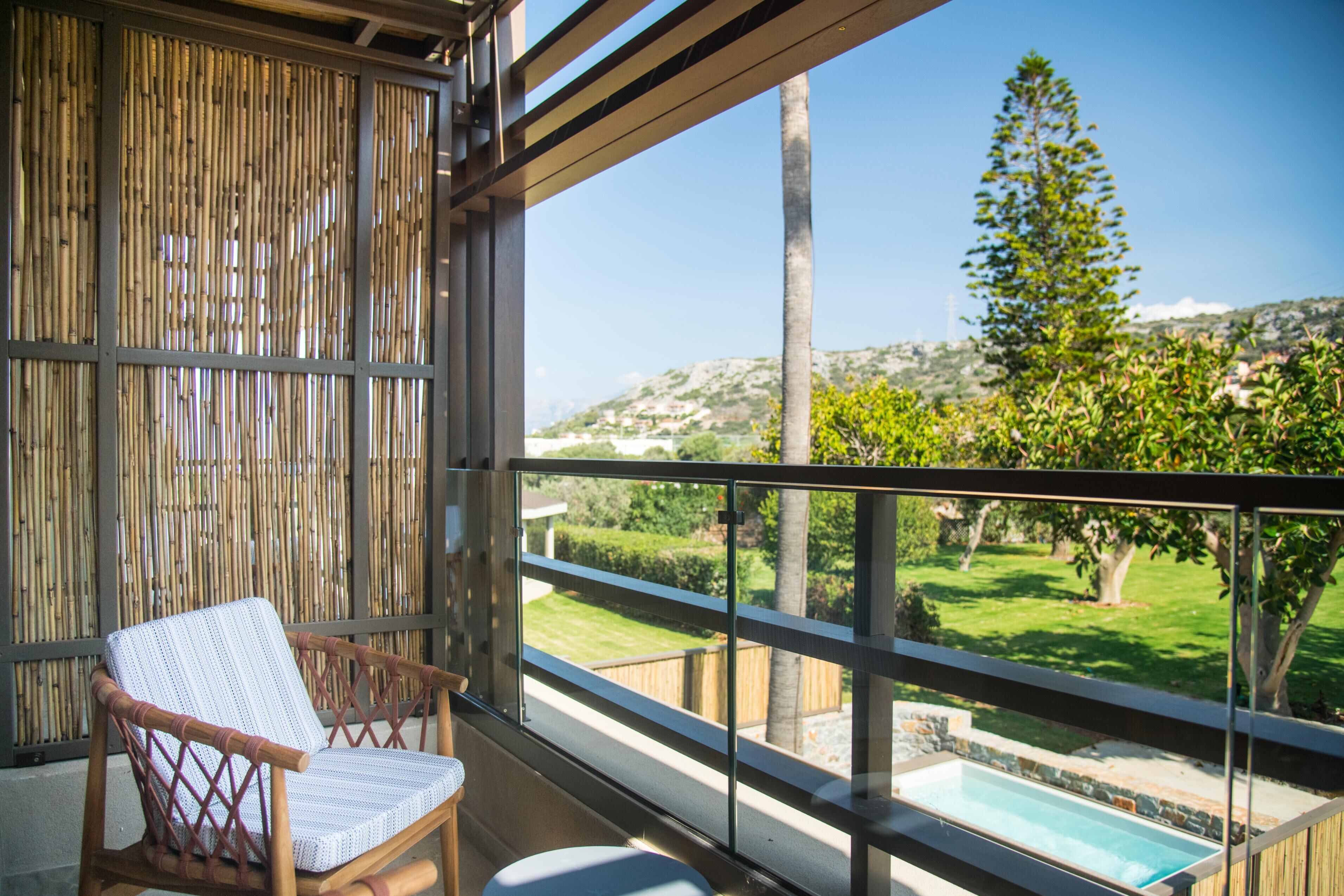 Uma varanda com cadeira de vime, vista para uma piscina e parede de bambu.