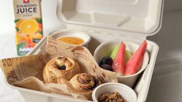 Recipiente de comida com suco em cartão, croissants, melancia, uvas e granola.