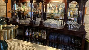 Uma área de bar com prateleiras cheias de garrafas de bebidas e copos.