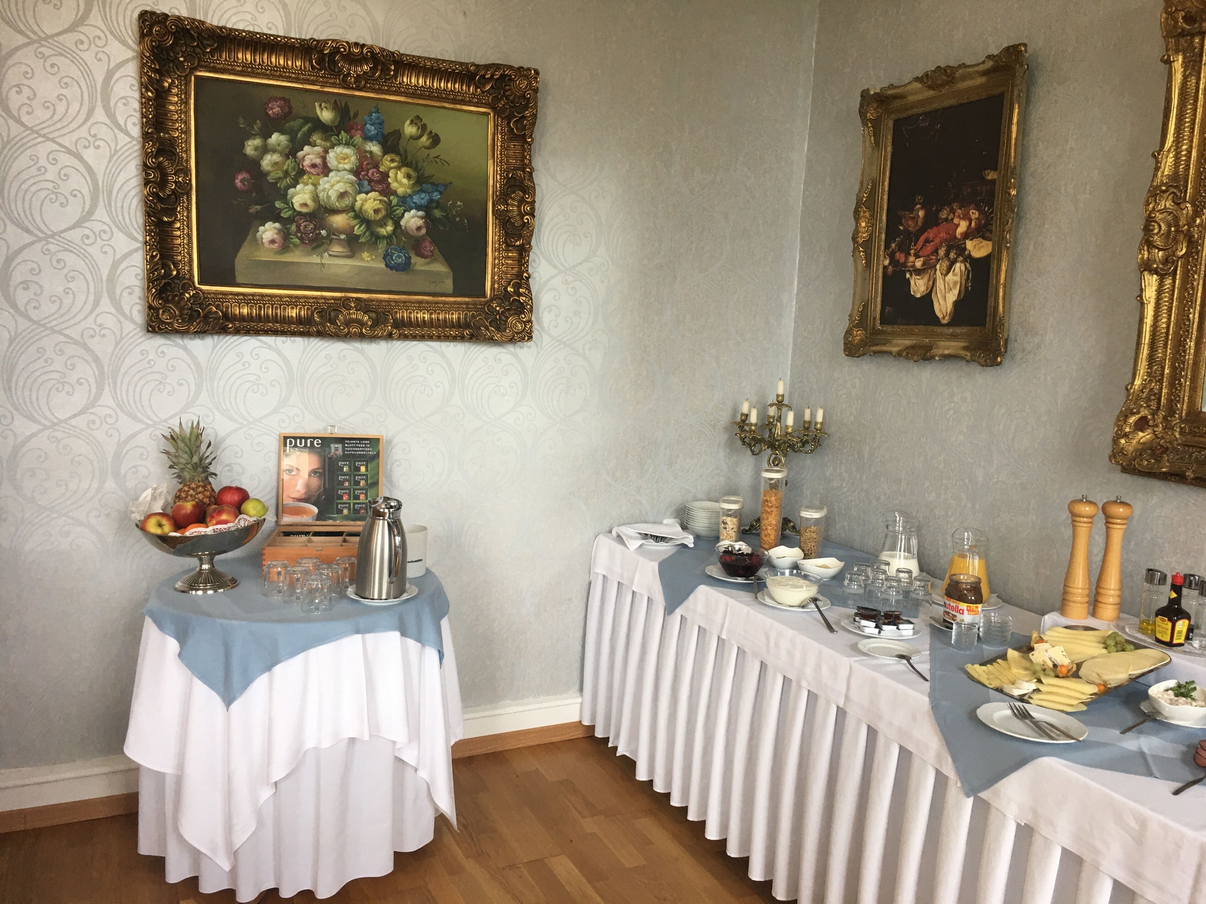 Uma sala de jantar com uma mesa posta para refeição, uma tigela de frutas, um coador de café e um quadro na parede.