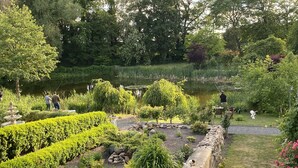 Um jardim bem cuidado com lago, sebes podadas e diversas plantas.