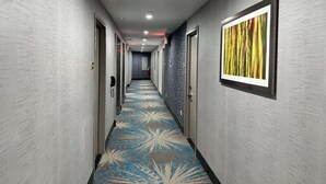 Um corredor com carpete estampado, portas e um quadro na parede.