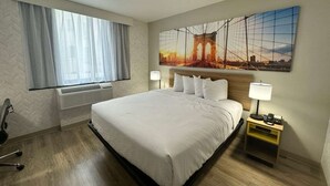 Quarto de hotel com uma cama grande, janela com cortinas finas, pintura pendurada na parede de uma ponte, mesa de cabeceira com abajur e uma cadeira.