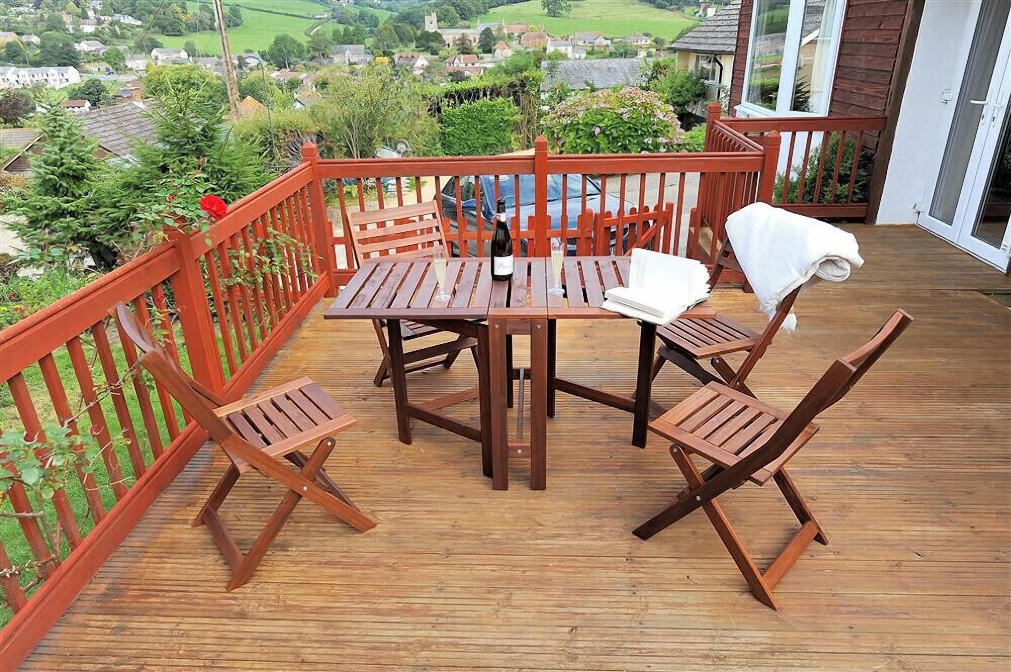 Um deck de madeira com uma mesa e cadeiras, com vista para uma paisagem verde.