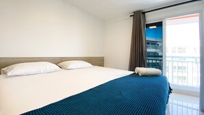 Quarto de hotel com uma cama, janela com cortinas e vista para um edifício.