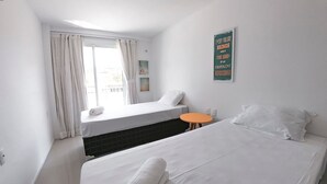 Quarto de hotel com duas camas, uma mesa pequena laranja e uma janela com cortinas.
