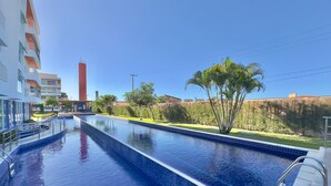 Uma piscina com um céu azul límpido, uma chaminé alta e avermelhada e um edifício com varandas.