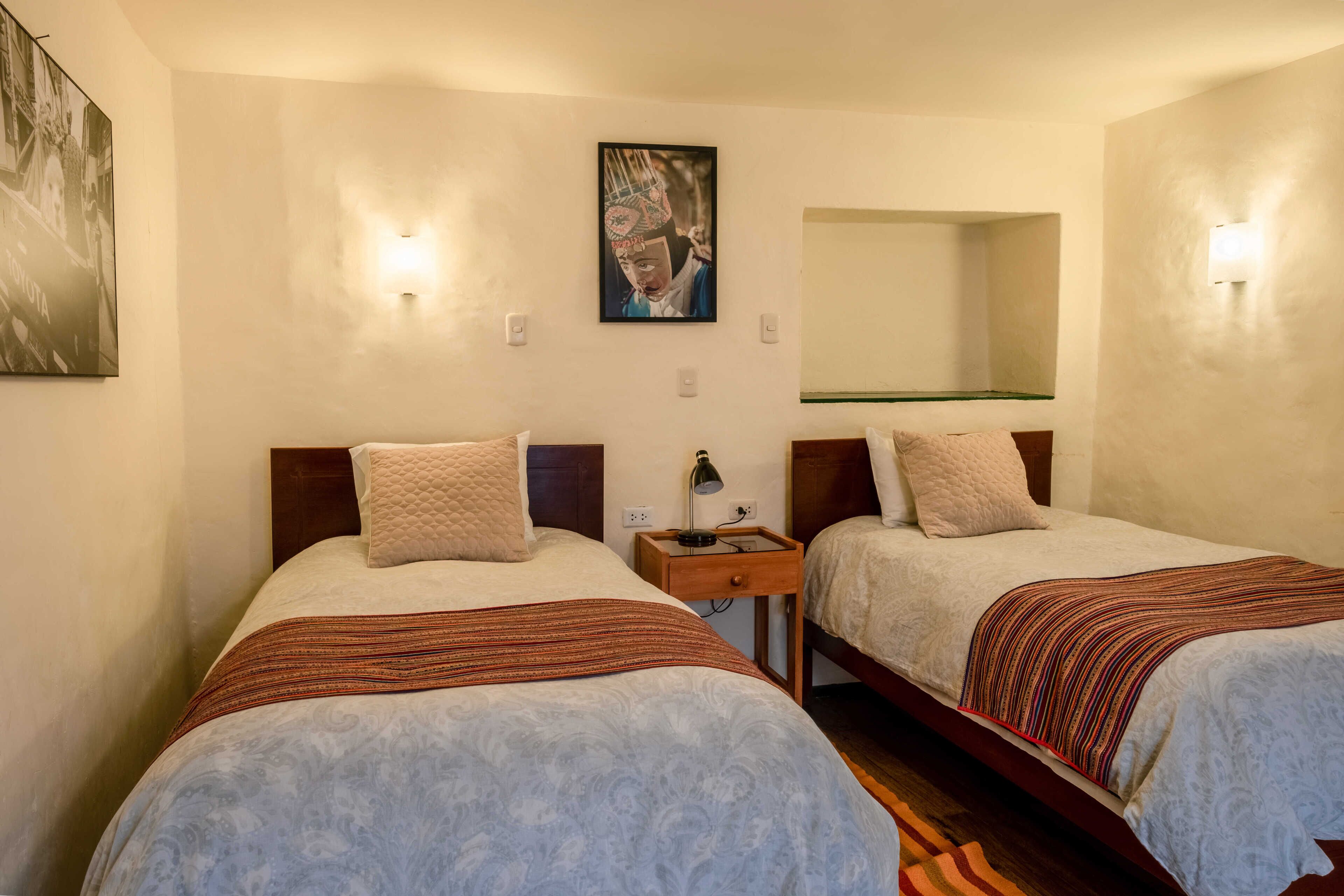 Quarto de hotel com duas camas, uma mesa de cabeceira, um abajur e um quadro na parede.