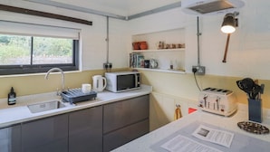 Uma cozinha compacta com pia, micro-ondas, torradeira e chaleira.