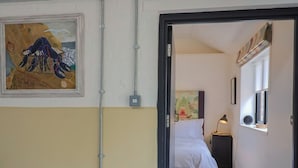 Quarto com cama, mesa de cabeceira, abajur e um quadro na parede.