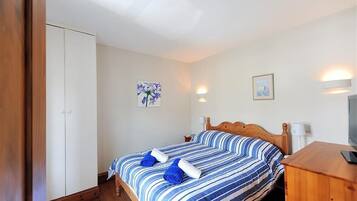 Quarto com cama, luminárias de cabeceira, mesa de cabeceira de madeira, televisão e guarda-roupa.