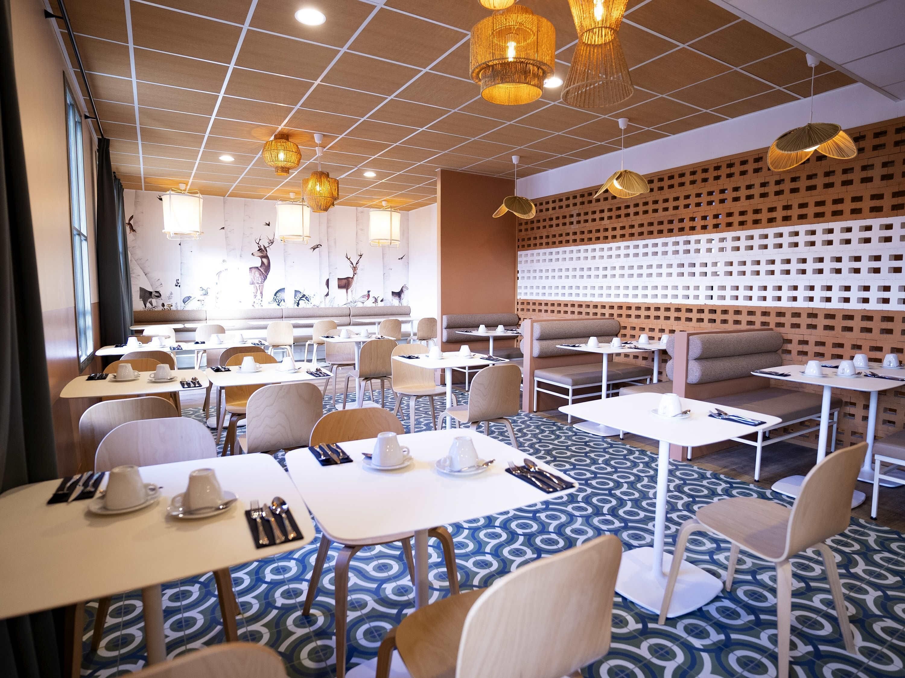 Um restaurante com mesas, cadeiras, piso estampado e luminárias pendentes.