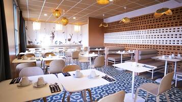 Um restaurante com mesas, cadeiras, piso estampado e luminárias pendentes.