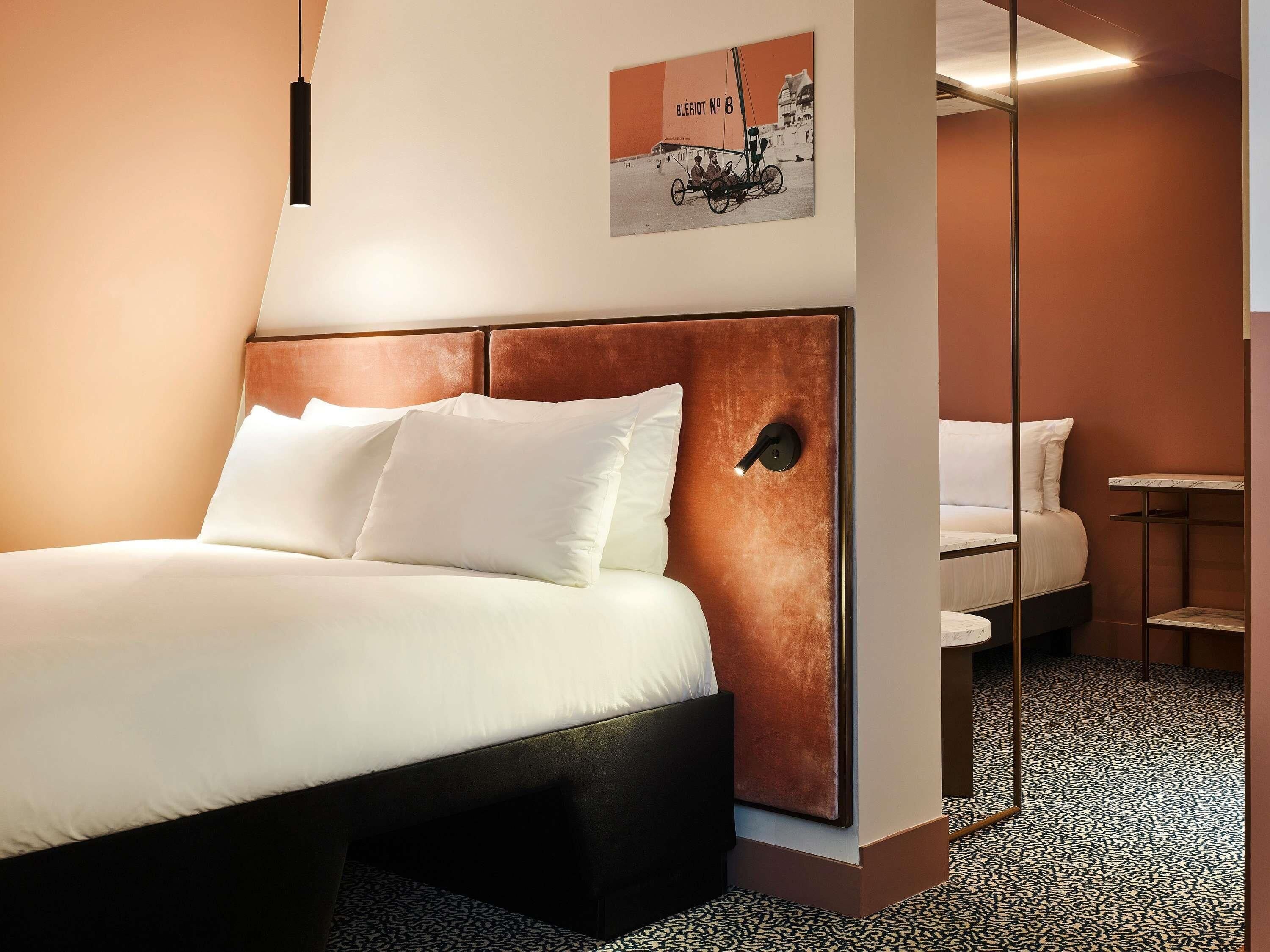 Quarto de hotel com cama, cabeceira, mesa de cabeceira, espelho e quadro na parede.