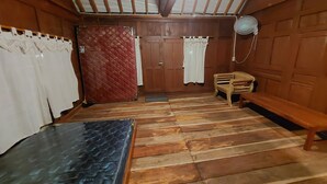 Um quarto com piso de madeira, um banco, uma porta vermelha e um ventilador de teto.