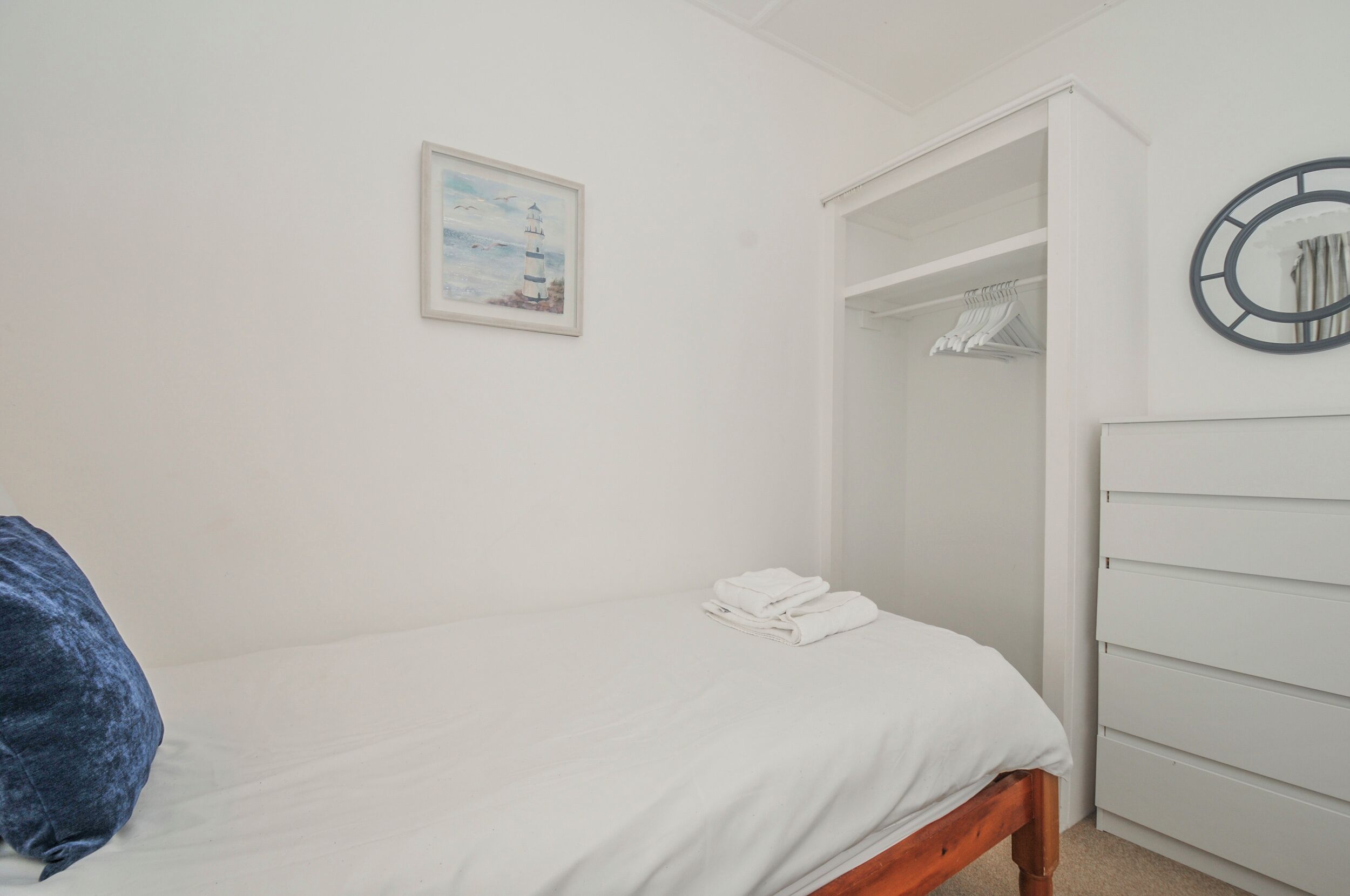 Quarto com cama, guarda-roupa, cabideiro e um quadro de um farol.