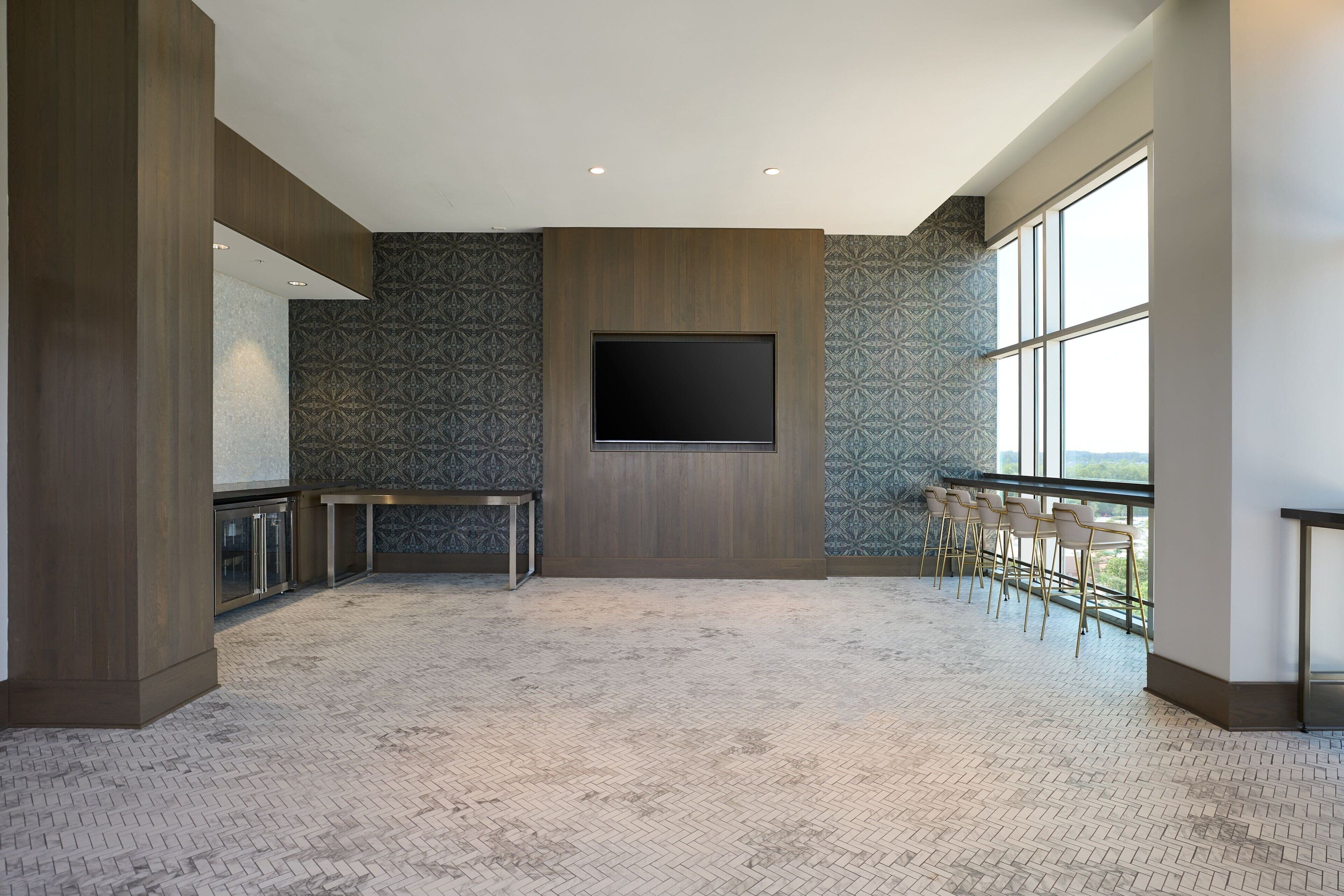 Um quarto amplo com uma grande TV de tela plana fixada em uma parede de madeira, um espaço de bar com banquetas e um piso estampado.