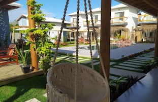 Uma área externa coberta com uma cadeira suspensa, uma piscina e um jardim.
