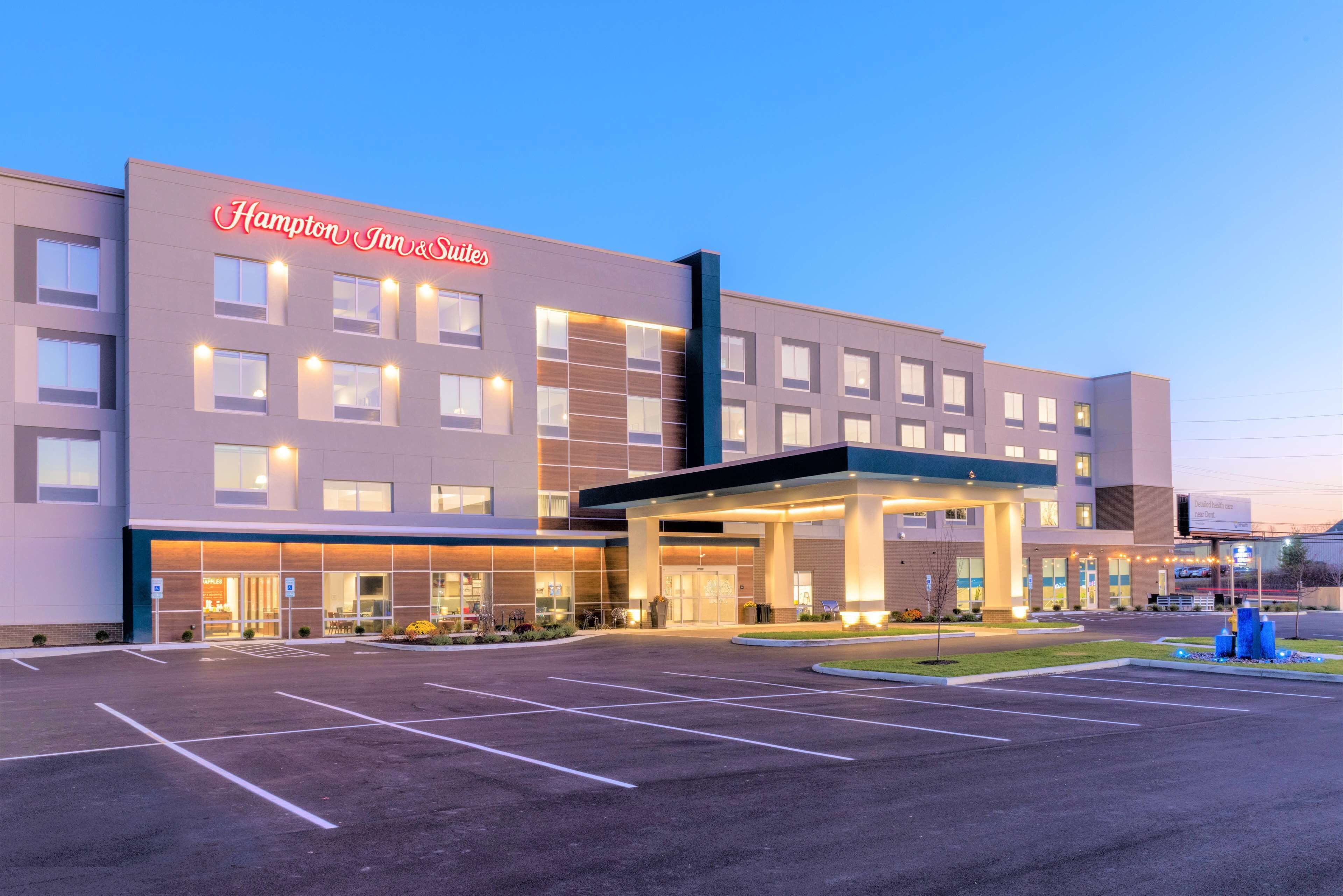 Um hotel Hampton Inn & Suites com fachada moderna, vários acessos e um amplo estacionamento.