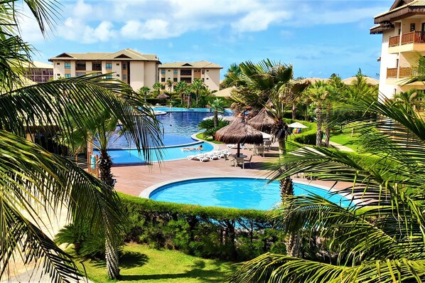 Resort com várias piscinas, palmeiras e estruturas com telhado de palha.