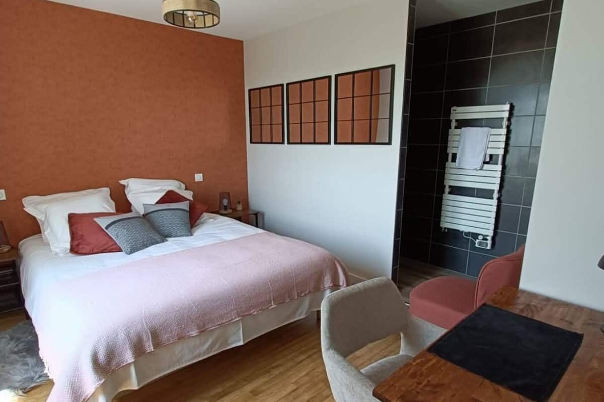 Quarto com cama, mesas de cabeceira, uma cadeira, uma mesinha e porta-toalhas fixado na parede.