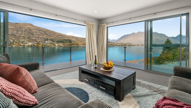 Sala de estar moderna com uma grande janela com vista para um lago e montanhas.
