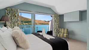 Quarto com cama grande, uma cadeira e vista para um corpo d'água e colinas.