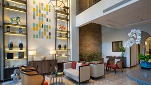 Um hall moderno com teto alto, área de estar central com sofás e poltronas, parede decorativa com padrão em mosaico e uma grande orquídea em vaso.