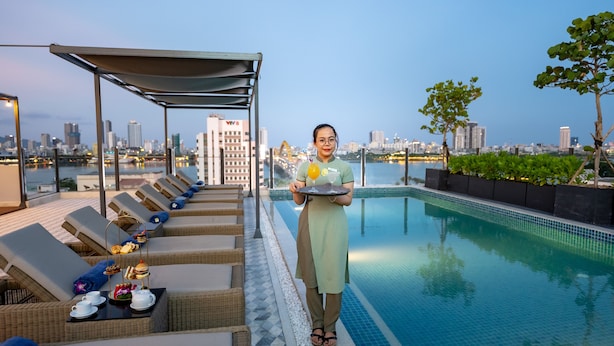 Área da piscina com espreguiçadeiras, uma bandeja de comes e bebes, e vista panorâmica da cidade ao fundo.