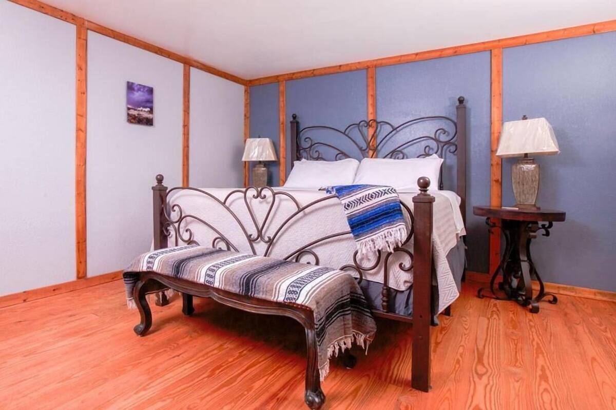 Quarto com cama de madeira, duas mesas de cabeceira com abajures e um banco aos pés da cama.