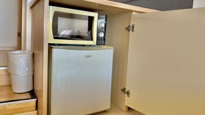 Uma cozinha compacta com micro-ondas e geladeira, uma lixeira e um armário de madeira.