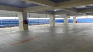 Uma ampla garagem com pisos e colunas de concreto, corrimãos de metal e paredes azuis.