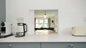 Cozinha com cafeteira, torradeira e vista para uma sala de jantar com mesa e cadeiras.