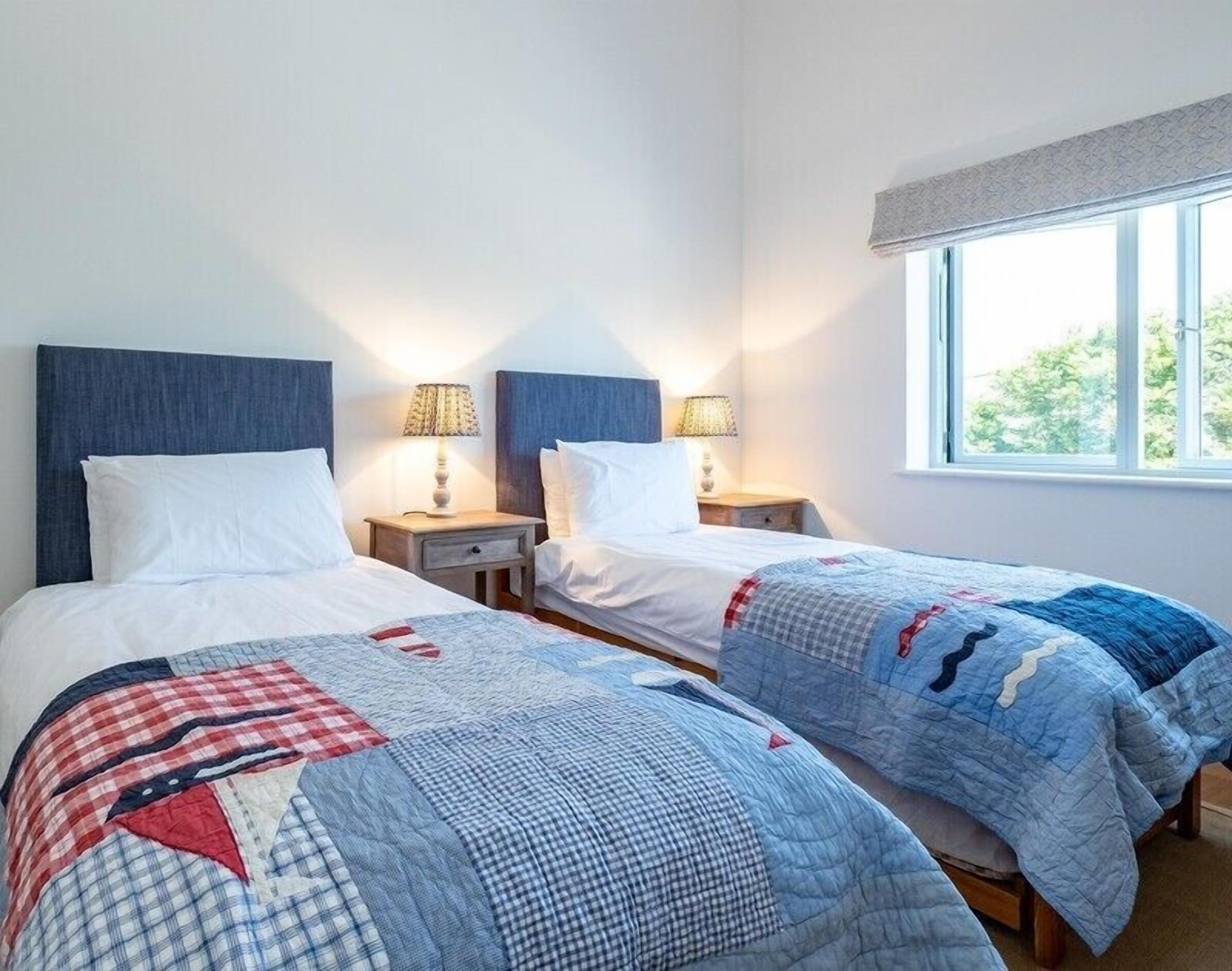 Quarto com duas camas, cada uma com um edredom diferente, uma janela com vista e luminárias laterais.