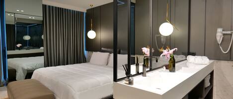 Quarto de hotel moderno com uma cama grande, toucador com espelho e banheiro separado.