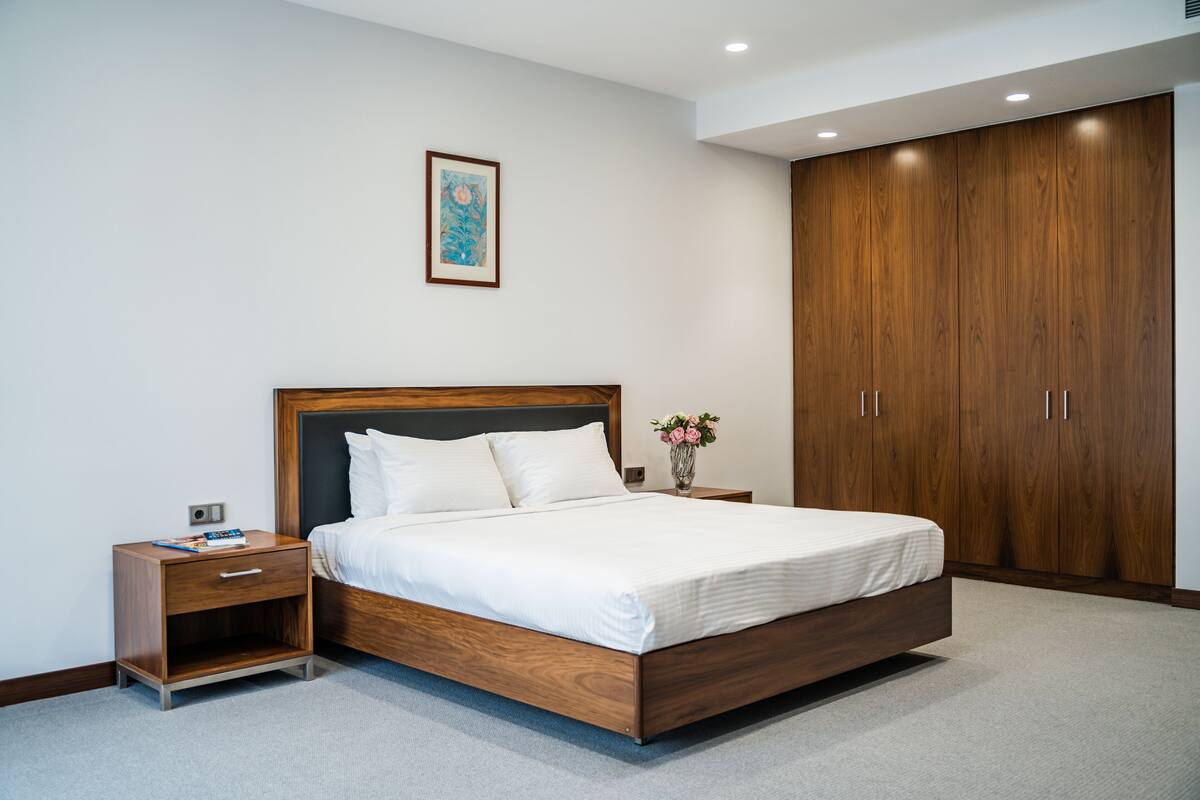 Um quarto moderno com uma cama de madeira, uma mesa de cabeceira, um guarda-roupa espaçoso e um quadro na parede.