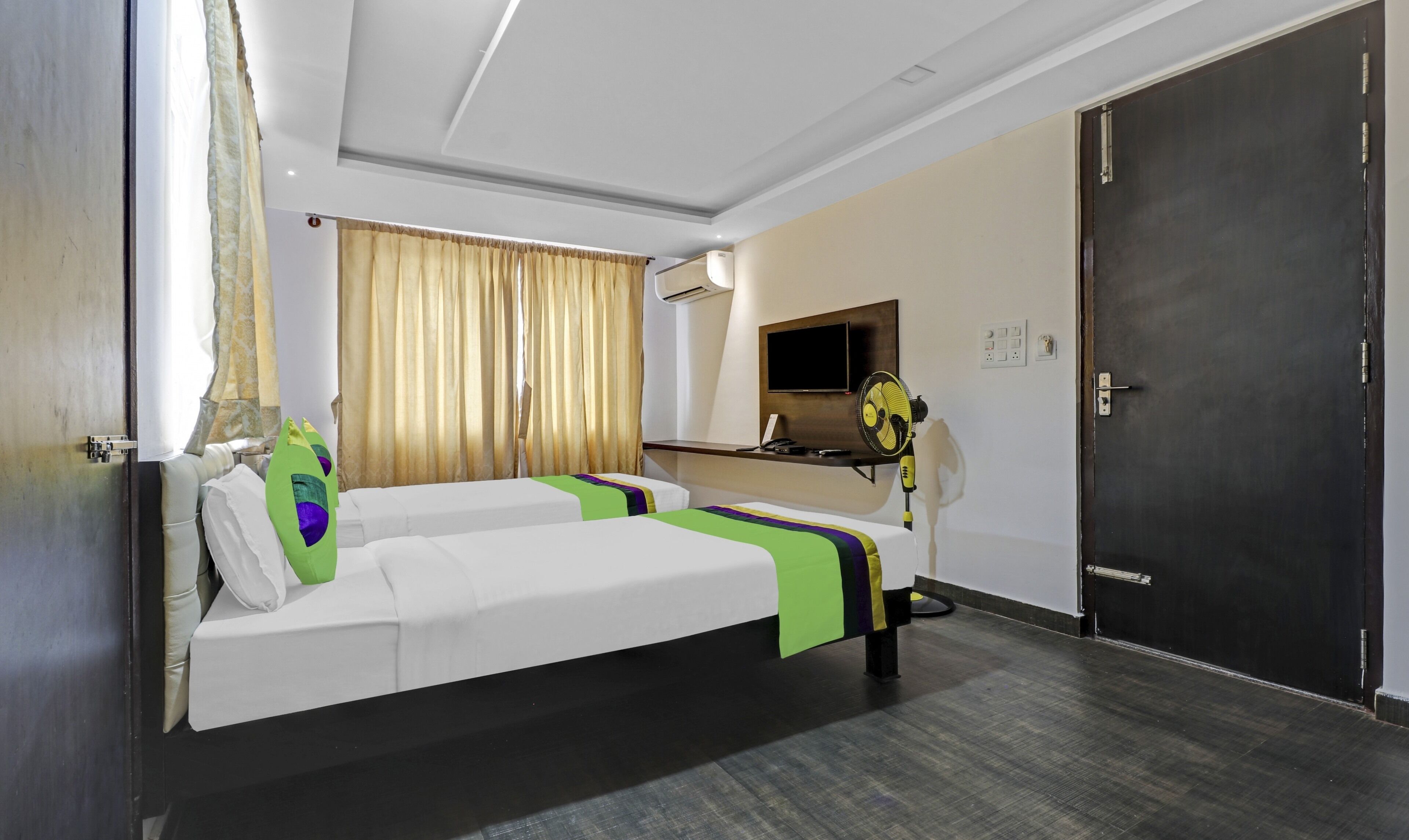 Quarto de hotel com cama, escrivaninha, televisão e ar condicionado.