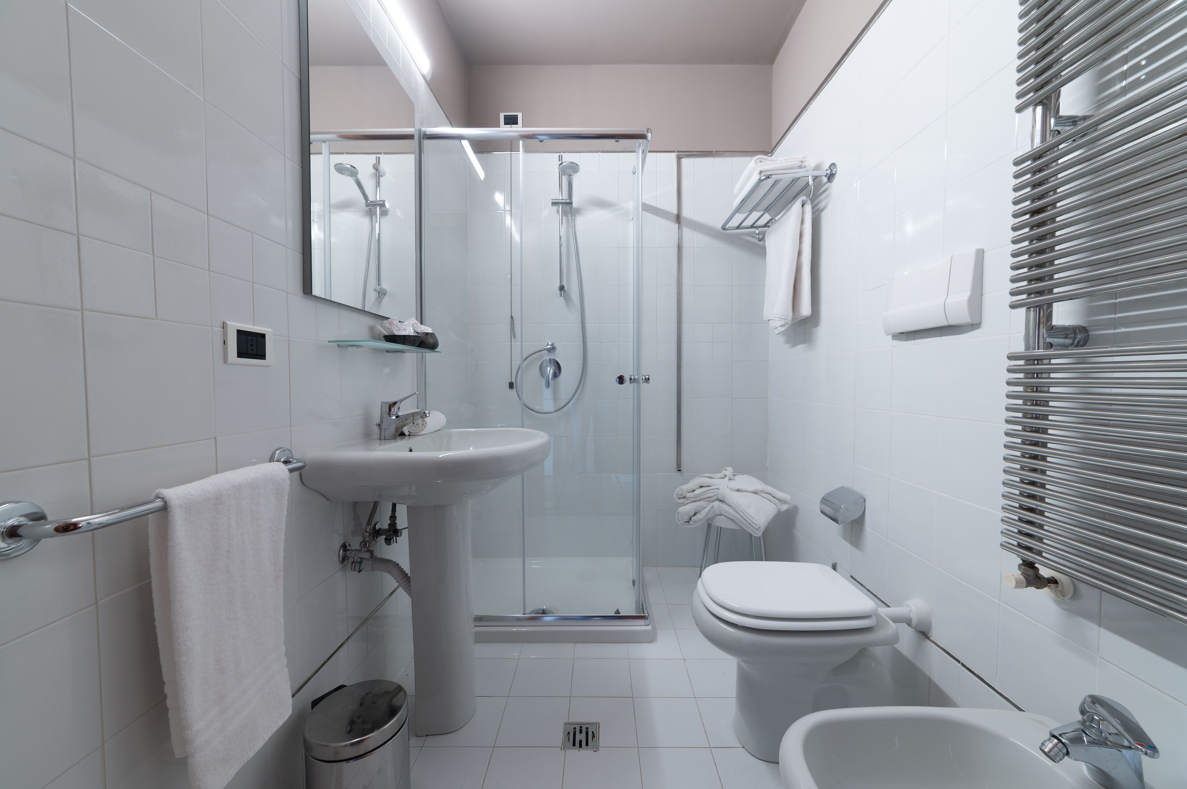 Um banheiro moderno com chuveiro de vidro, pia em pedestal, vaso sanitário e bidê.