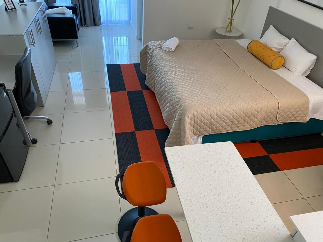 Quarto de hotel com uma cama, uma escrivaninha, uma cadeira de escritório e uma mesinha.
