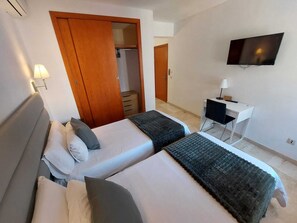 Quarto de hotel com duas camas, uma mesa, uma cadeira, uma televisão e um guarda-roupa.