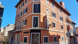 Um edifício de vários andares com fachada laranja marcante, várias janelas com persianas e uma entrada protegida por grades.