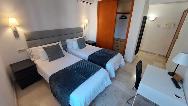 Quarto de hotel com duas camas, uma escrivaninha, uma cadeira e um guarda-roupa.