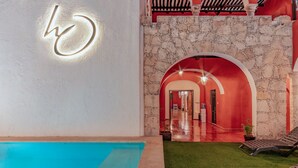 Entrada de hotel com piscina, parede de pedra e decoração em vermelho.
