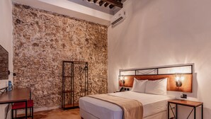 Um quarto com parede de pedra, cama com cabeceira de madeira, mesas de cabeceira e uma escrivaninha com cadeira.