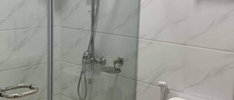 Casa de banho com chuveiro em cabine de vidro, sanita e porta-toalhas.