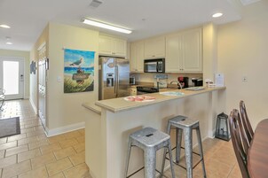 Uma cozinha com ilha central, eletrodomésticos de aço inoxidável e uma pintura de uma cena praiana.