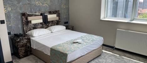 Quarto com cama, mesas de cabeceira, janela e parede com desenho de relógio.