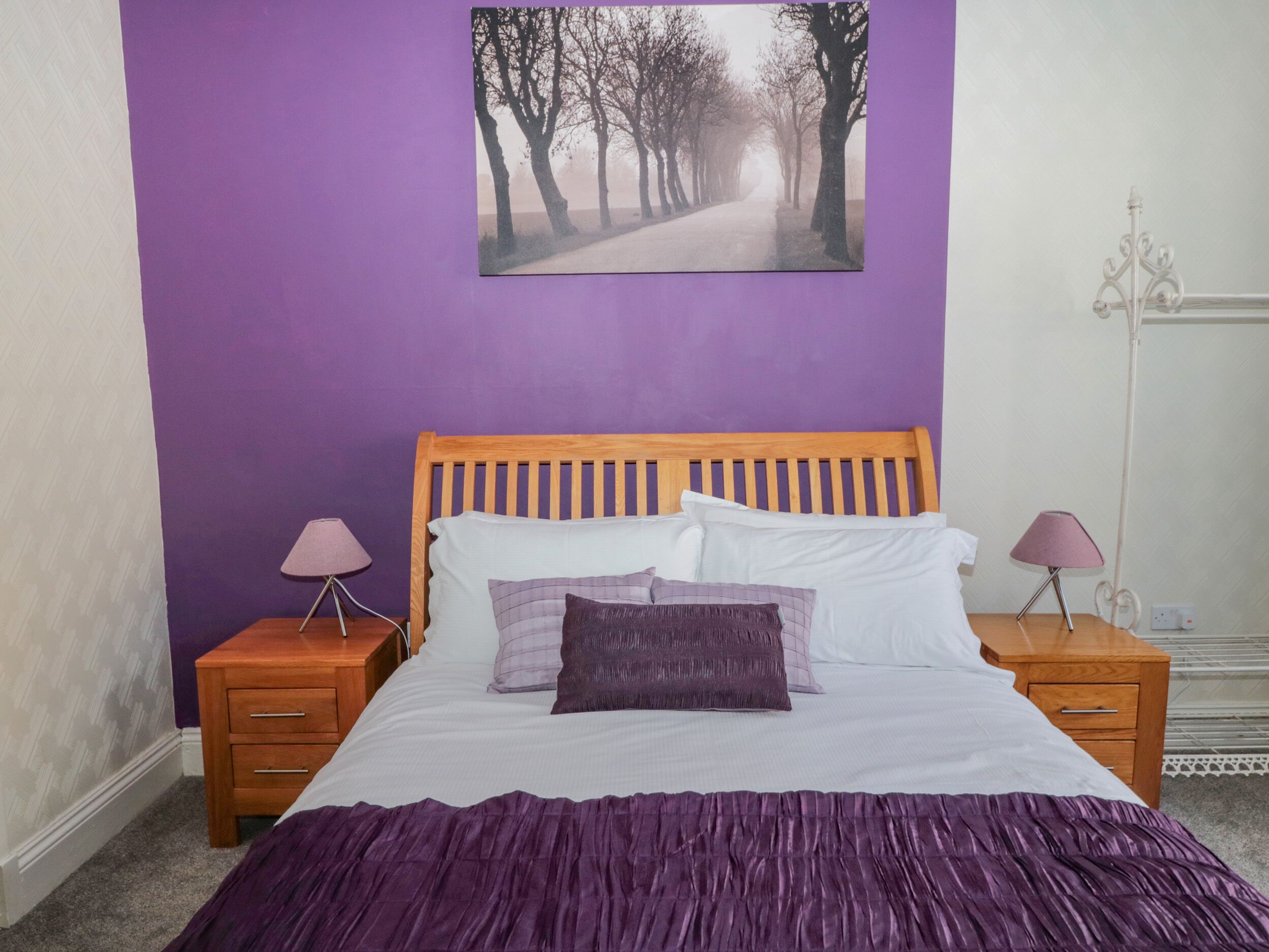 Quarto com cama de madeira, paredes roxas e um quadro com árvores.